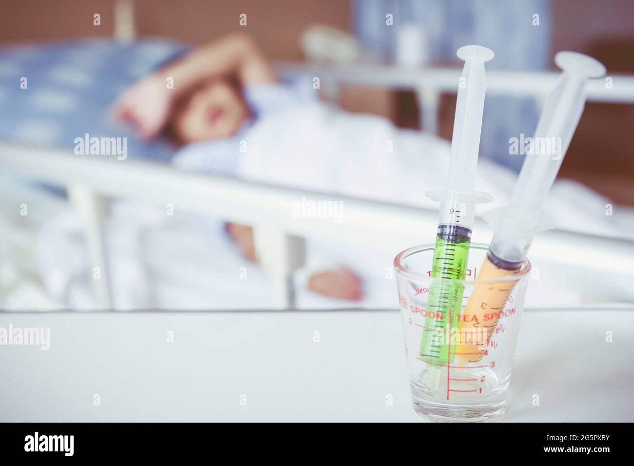 Syringes in a glass measuring cup with blurred illness boy lying on ...