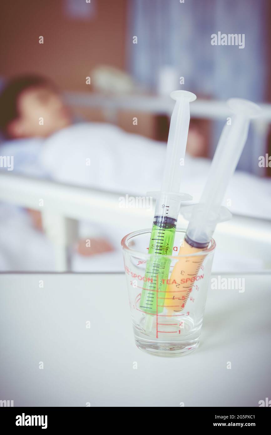 Syringes in a glass measuring cup with blurred illness boy lying on ...