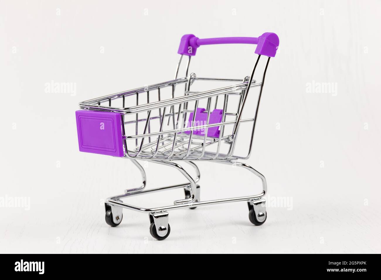 empty metal shiny grocery cart on wheels on white wooden table ...