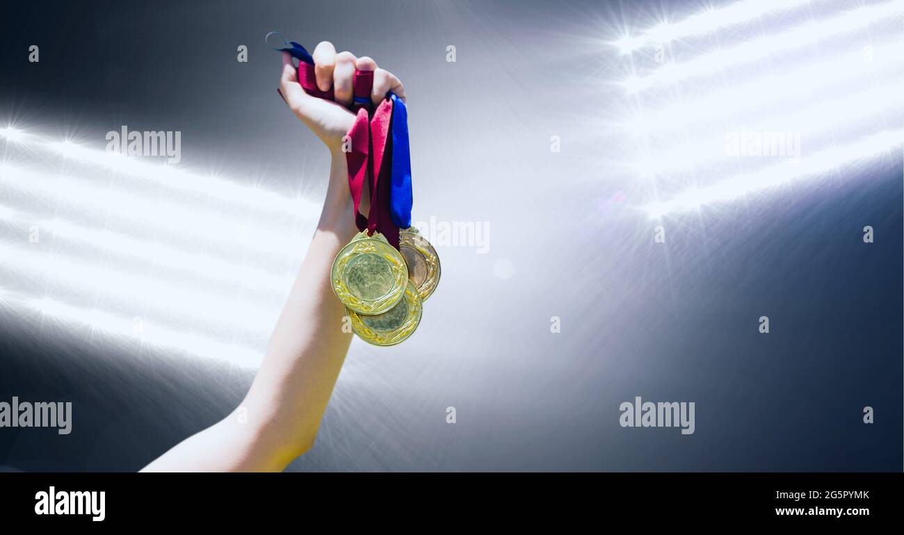 Close up of hand holding multiple medals against flood lights on black ...