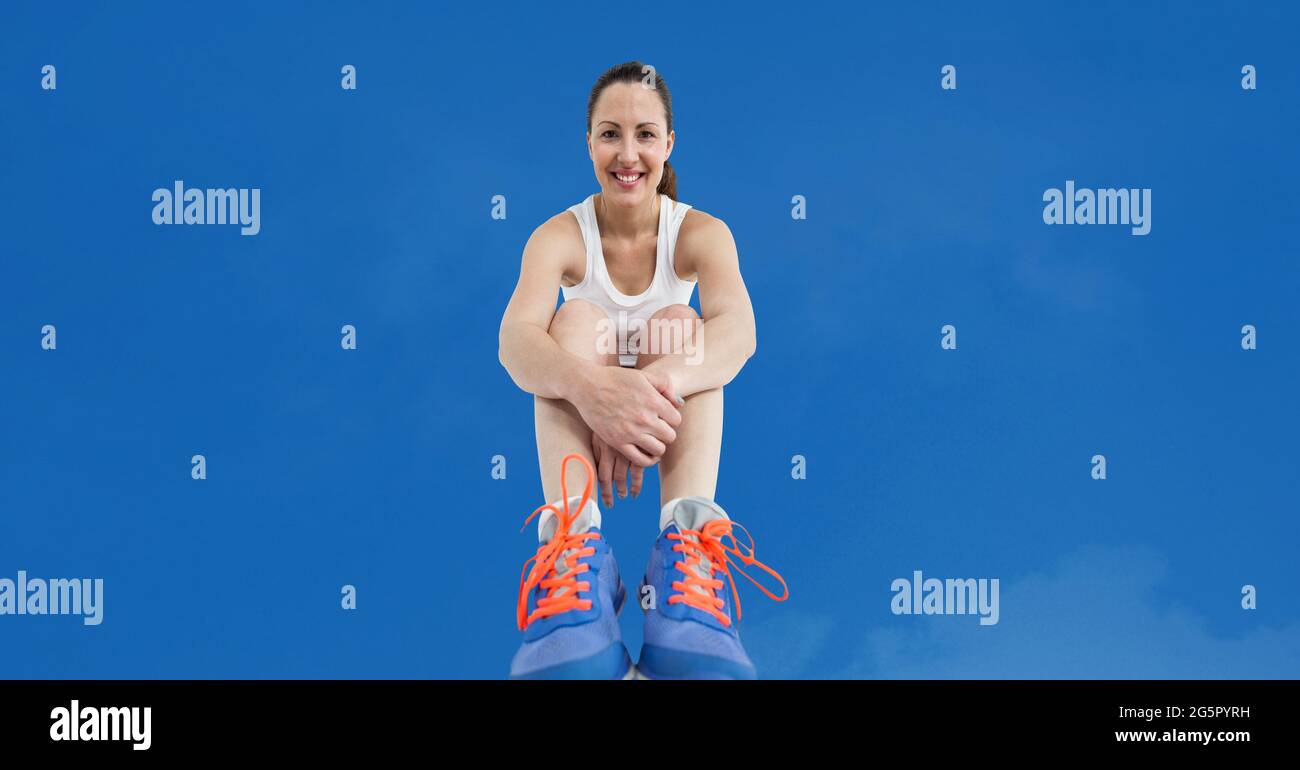 Portrait of caucasian female athlete smiling while sitting against blue ...