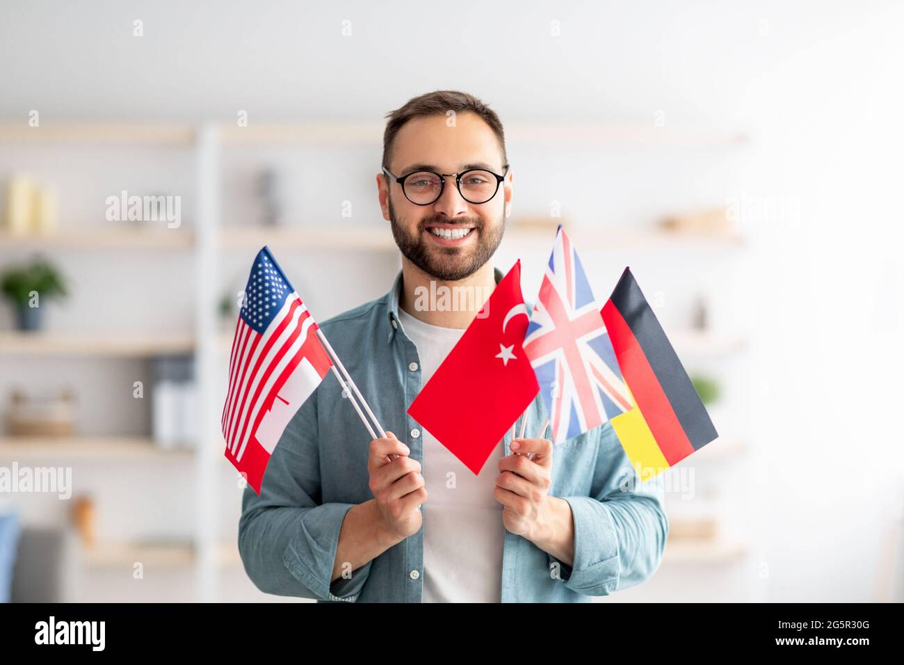 Handsome young guy holding bunch of diverse flags and smiling at camera ...