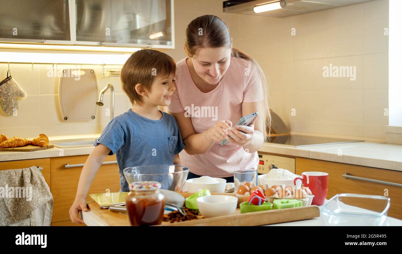 Happy little boy with young mother looking for new recipe to cook on ...
