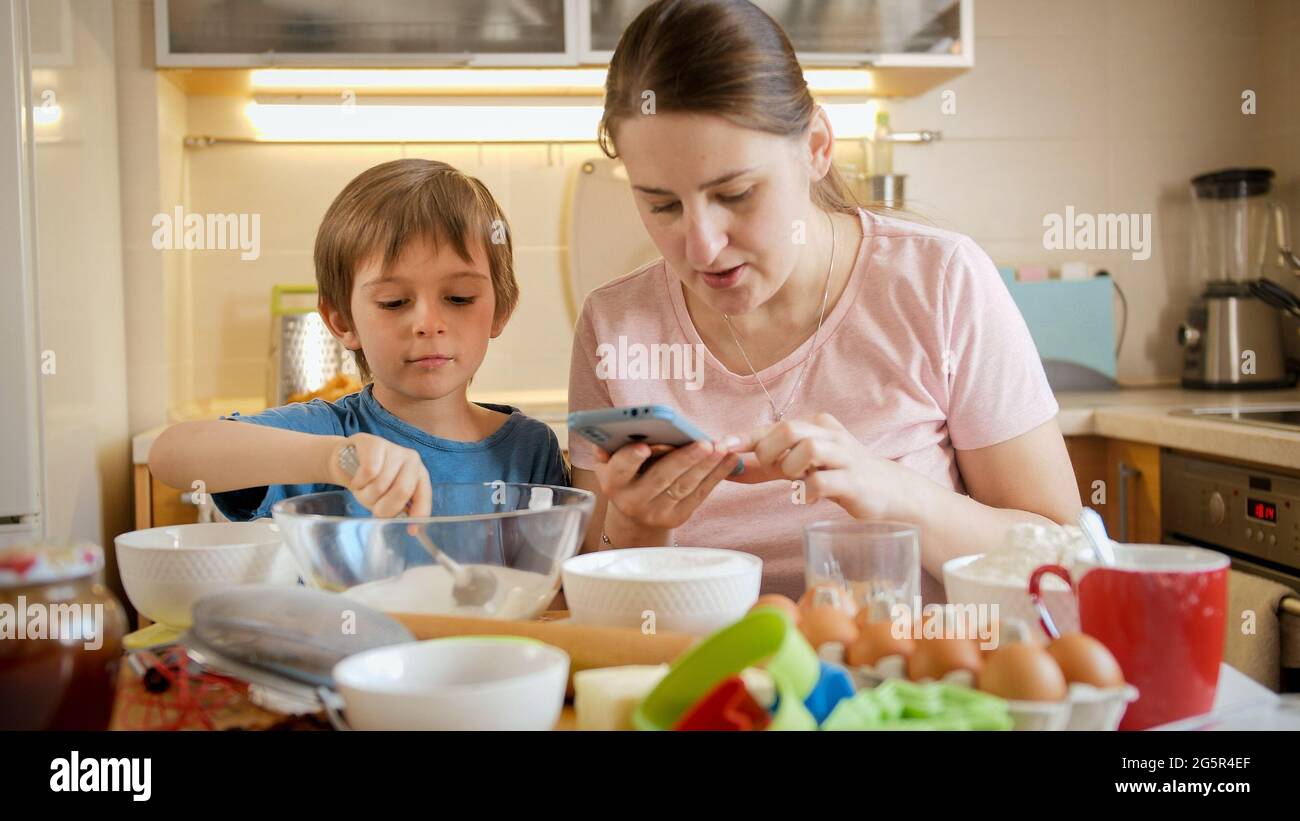 Happy smiling boy feeding mother from spoon while cooking pie or cake ...