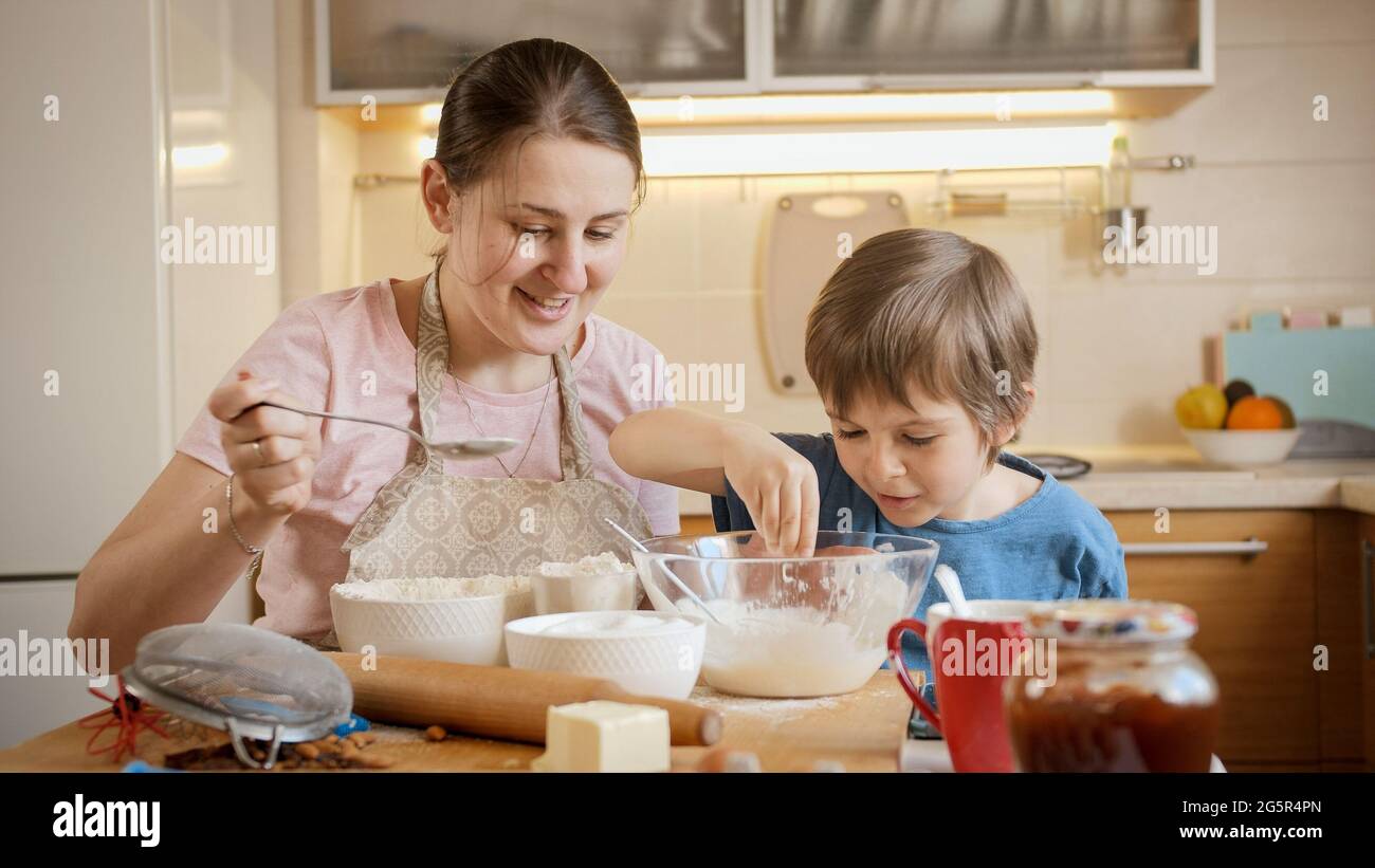 Smiling little boy with mother mixing ingredients in big bowl to make ...
