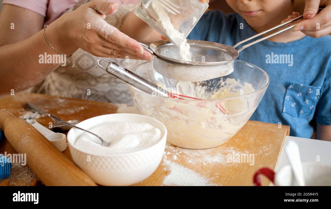 Closeup of little boy with mother sifting flour with sieve. Children ...