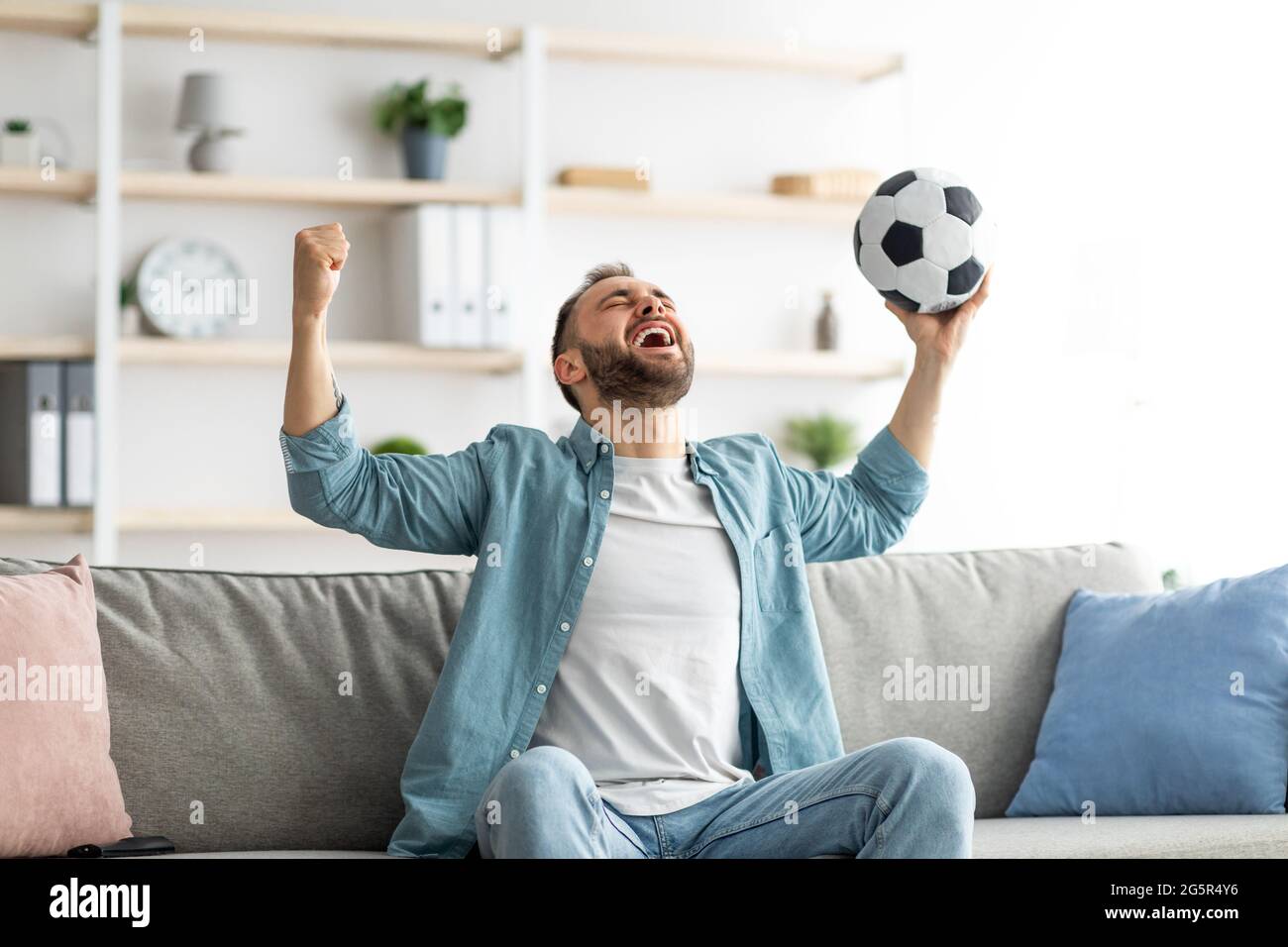 Emotional guy watching soccer on TV, lifting ball above his head and ...