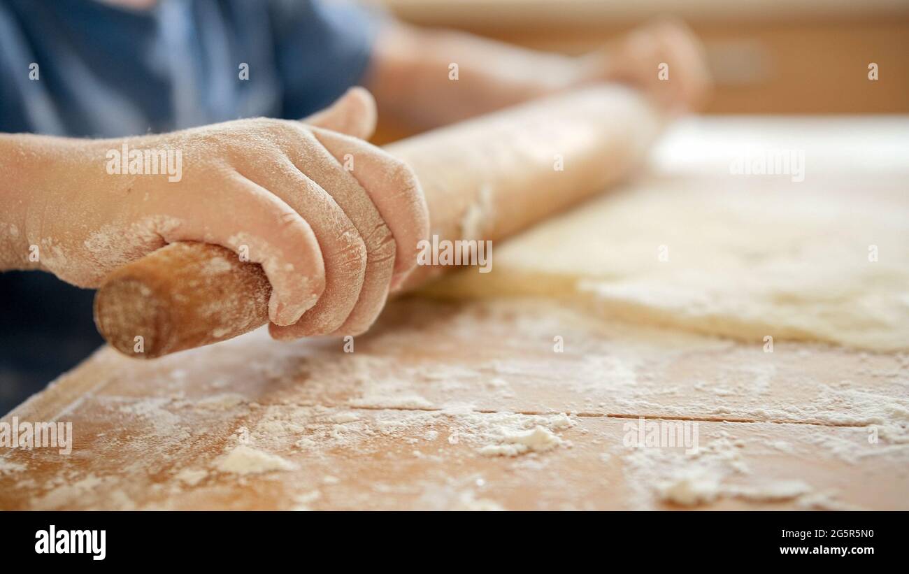 Closeup of little child using wooden rolling pin for preparing pizza ...