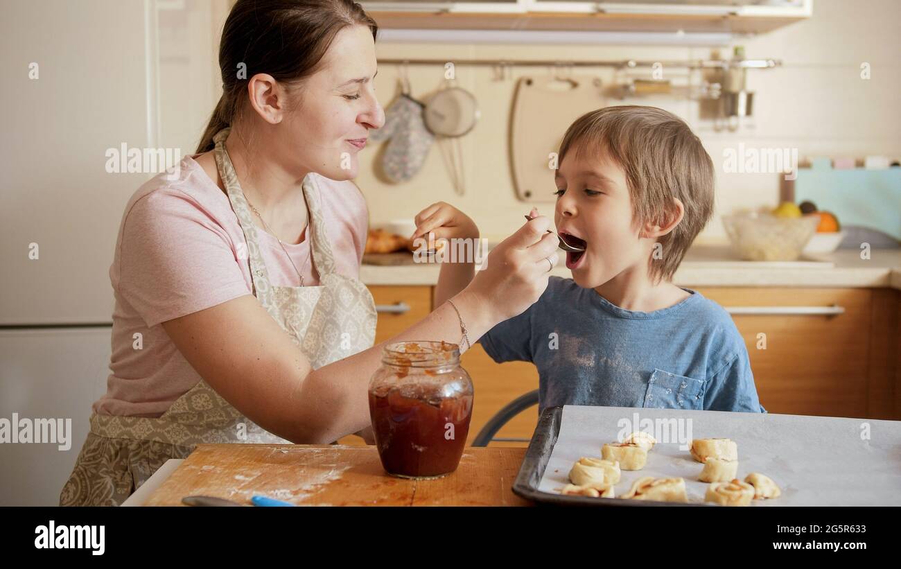 Happy smiling mother with little son eating sweet jam from jar while ...