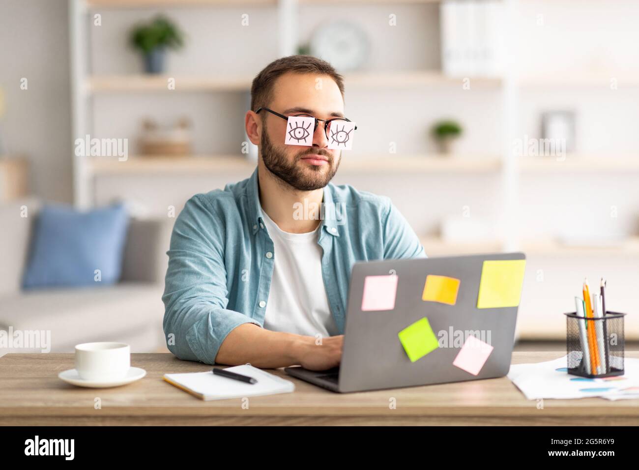 Tired millennial guy having stickers with drawings of open eyes on ...