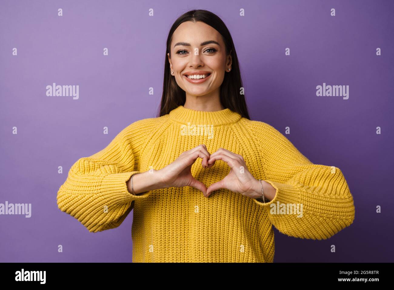 Happy young woman in sweater showing heart symbol with hands over ...