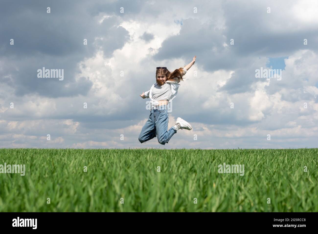 teen girl jumping in the green grass field, against the backdrop of the ...