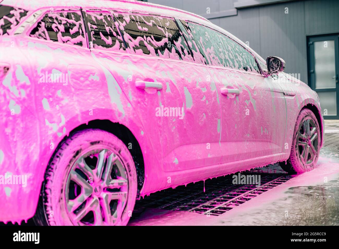 Car wash concept, Front view of white sports car covered with pink foam ...