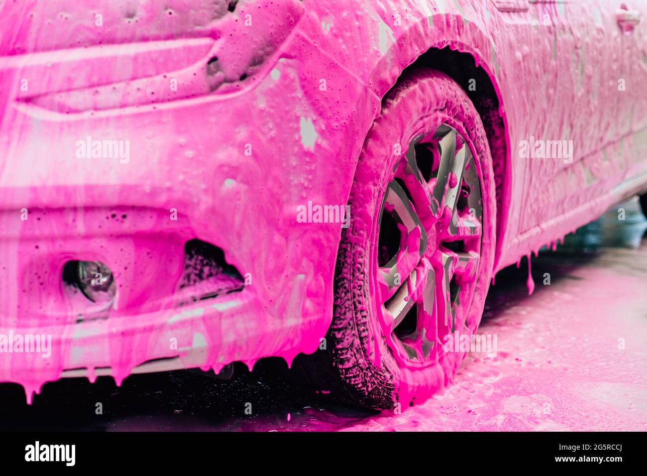 Car wash concept, Front view of white sports car covered with pink foam ...