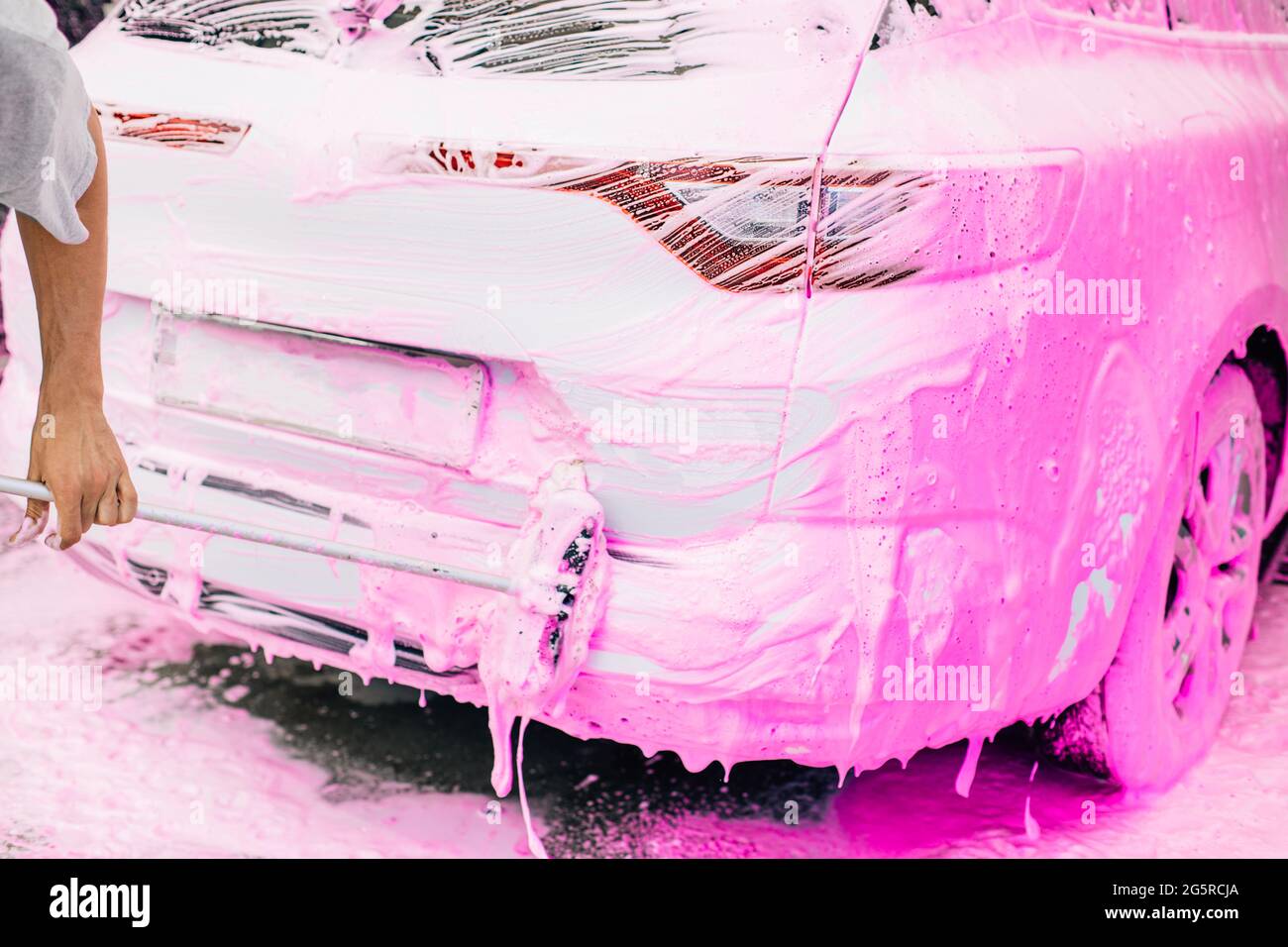 Car wash concept, Front view of white sports car covered with pink foam ...