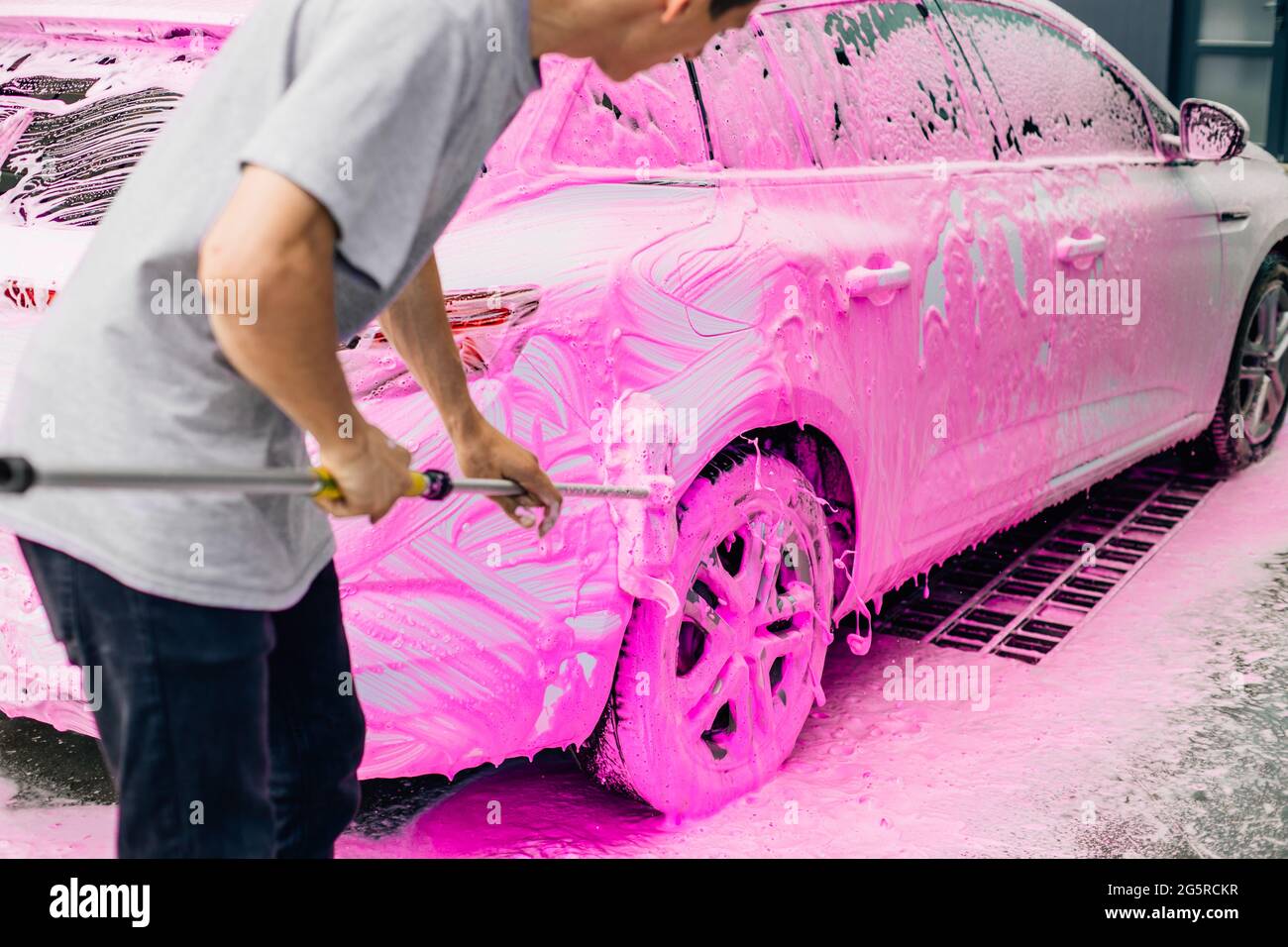 Car wash concept, Front view of white sports car covered with pink foam ...