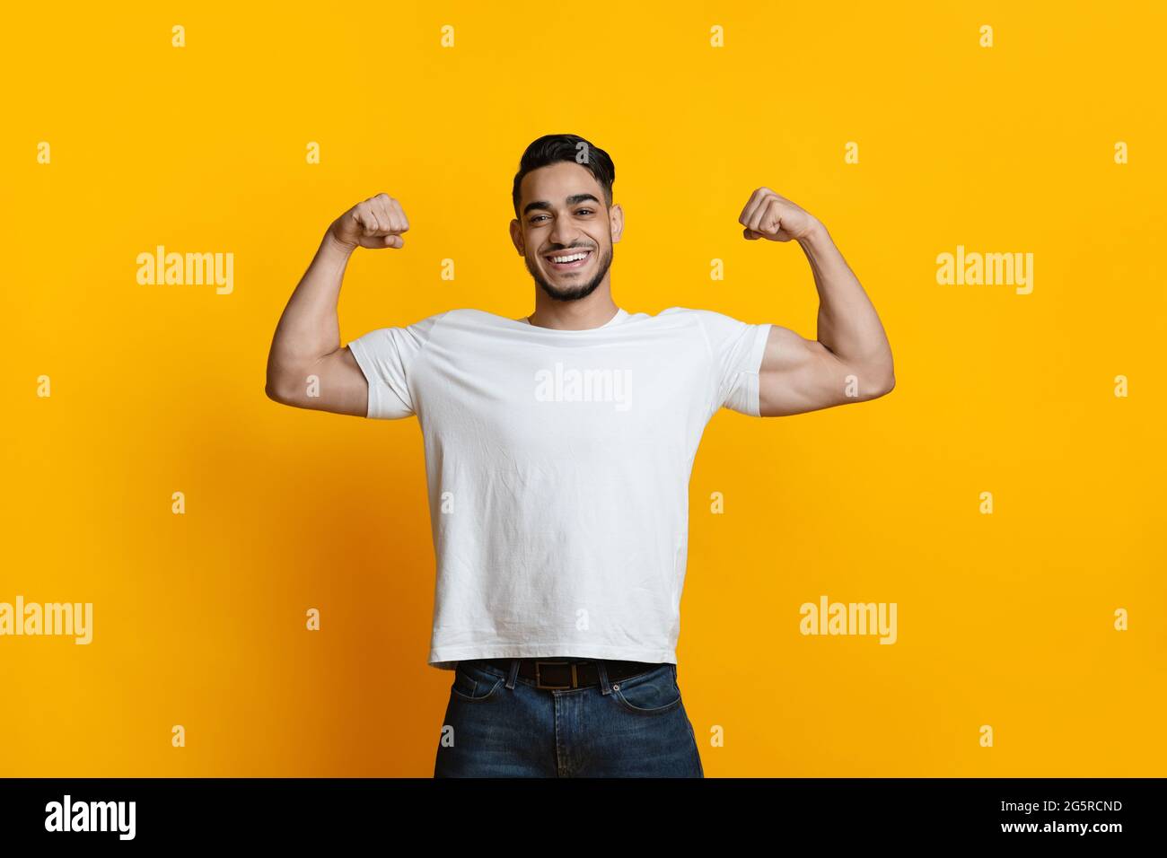 Smiling arab guy showing his biceps on yellow Stock Photo - Alamy