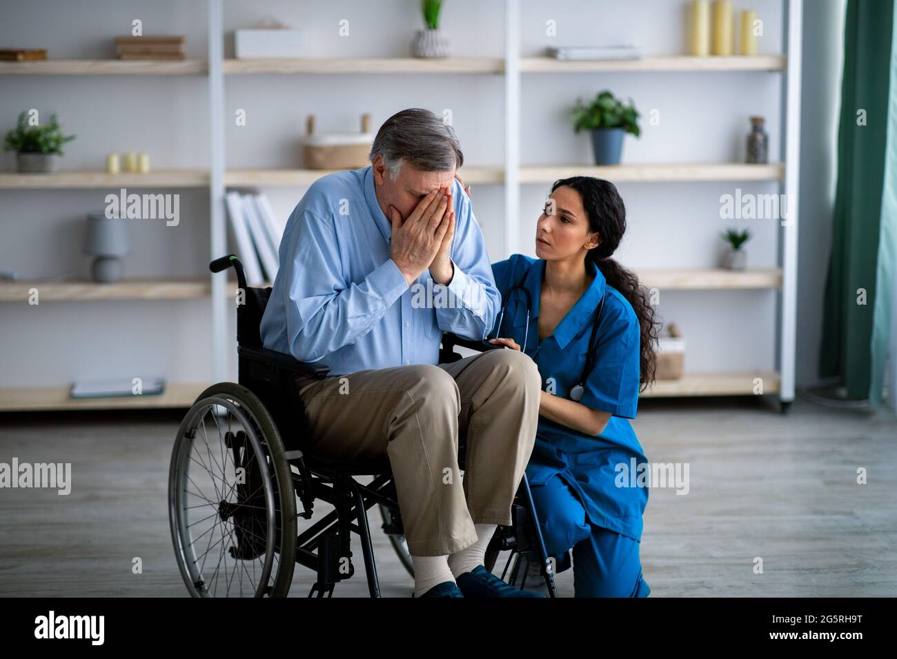 Depressed elderly male in wheelchair crying, young nurse consoling him ...