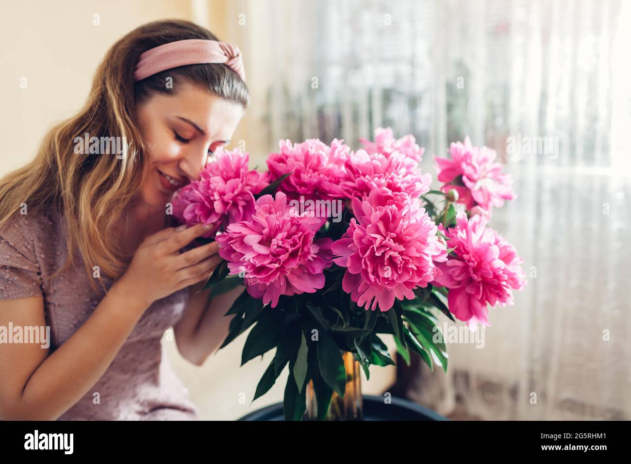 Woman smelling peonies flowers in vase at home. Girl enjoys bouquet of ...