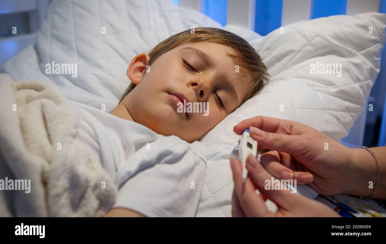 Mother looking at thermometer and checking body temperature of her sick ...