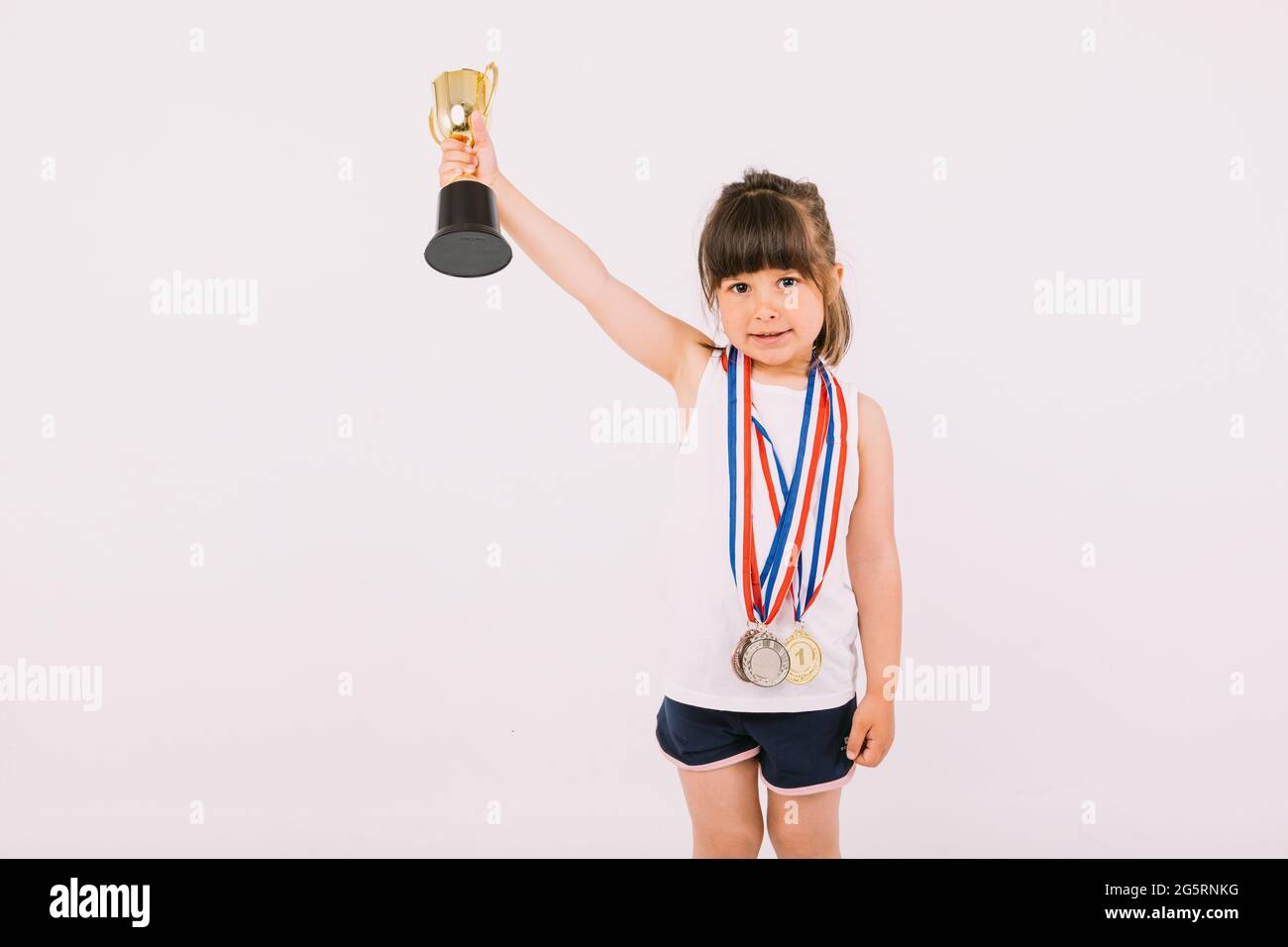 Little brown-haired girl with sports champion medals, lifting a trophy ...