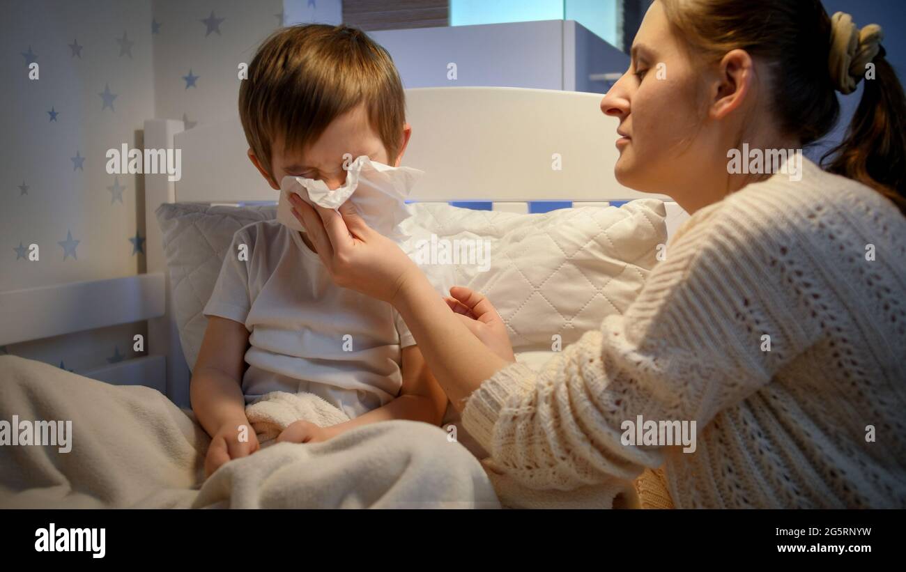 Little sick boy blowing nose in paper tissue and talking to mother ...