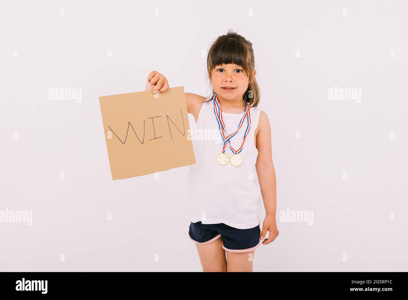 Small dark-haired girl with sports champion medals, holding a sign that ...