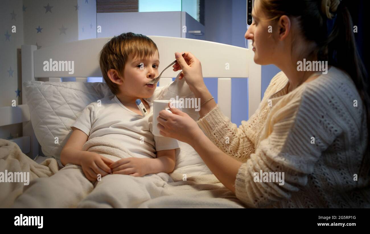 Little sick boy feeling unwell lying in bed and drinking medicines and ...