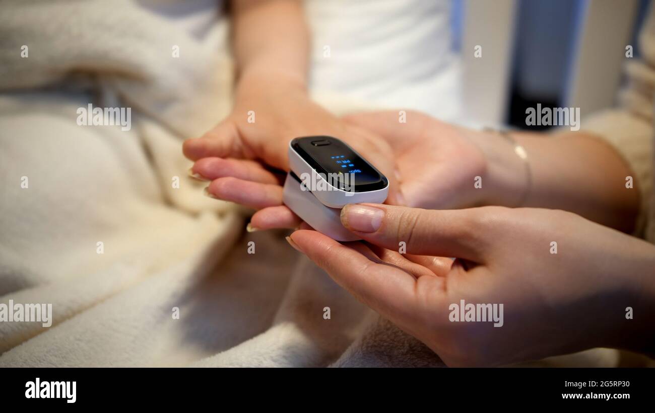 Woman using pulse oxymeter to measure oxygen level in blood of sick ...