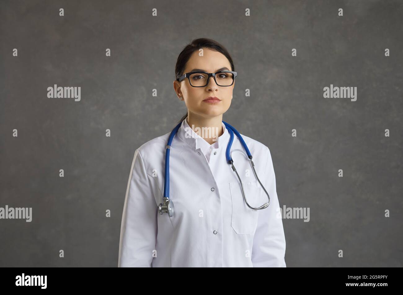Portrait of confident serious young female medical worker on gray ...