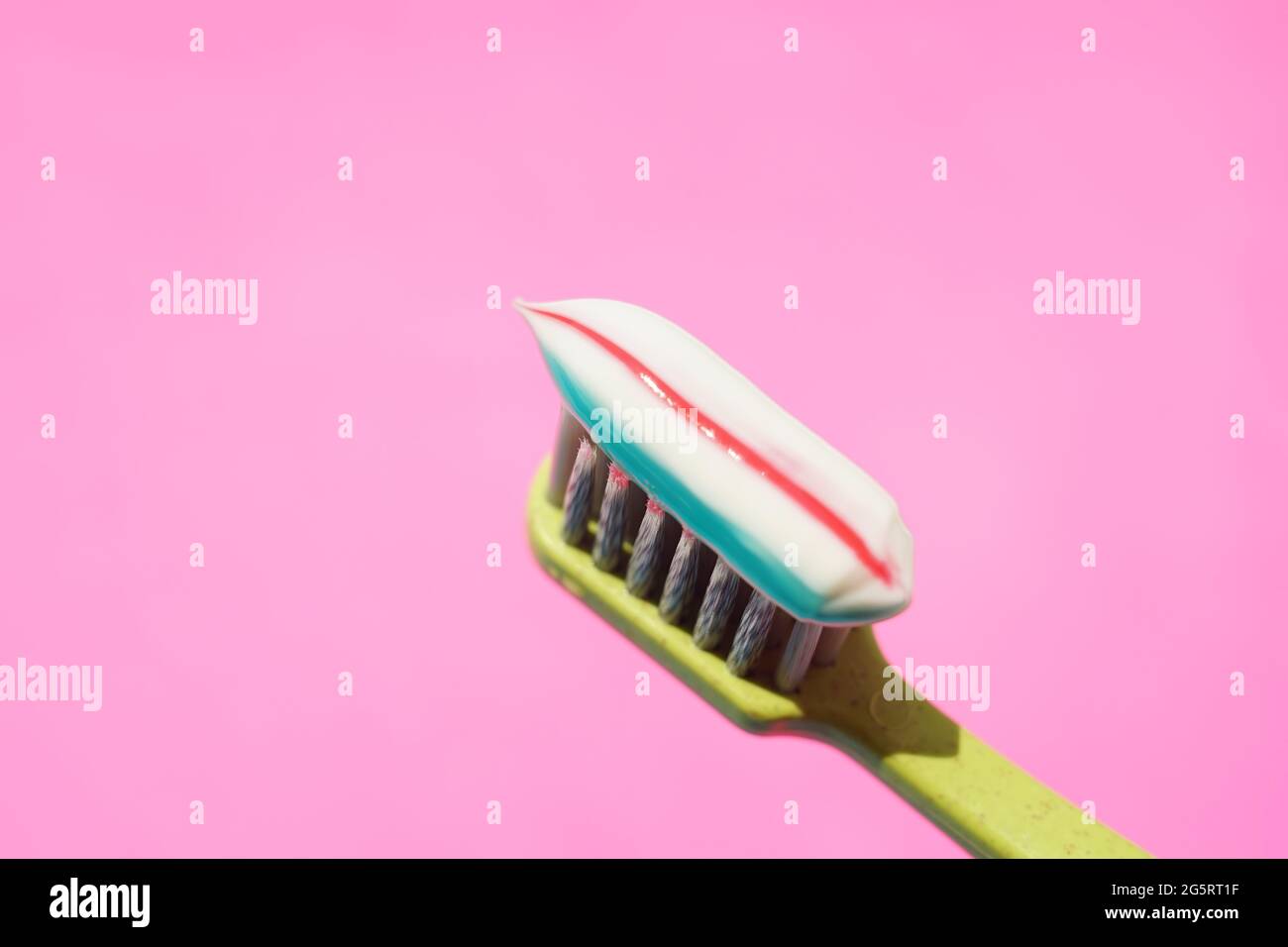 Green plastic toothbrush with striped toothpaste on pink background ...