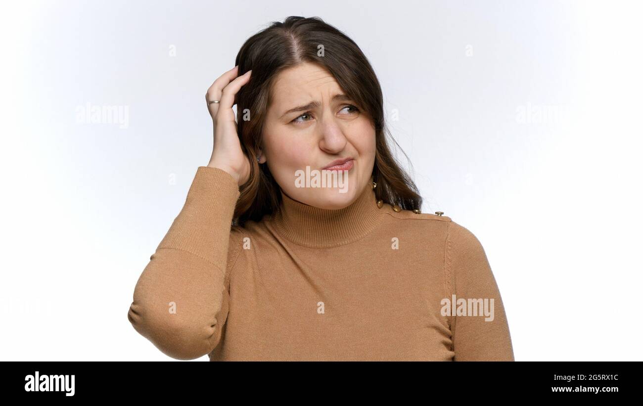 Studio portrait of thoughtful young woman thinking and rubbing her head ...