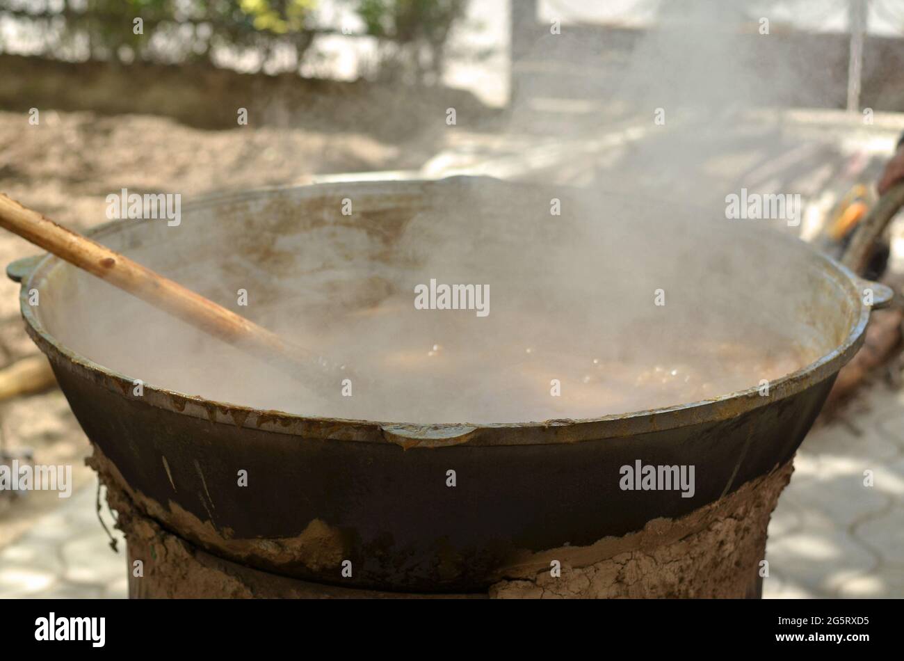Large black cauldron on the street, a brown food is cooked in it, steam ...