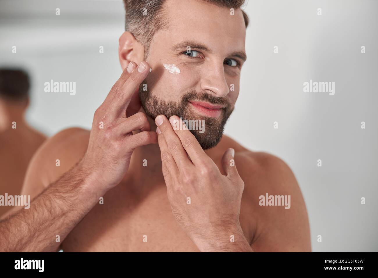 Happy man with stylish beard applies antiaging cream onto crowl feet on ...