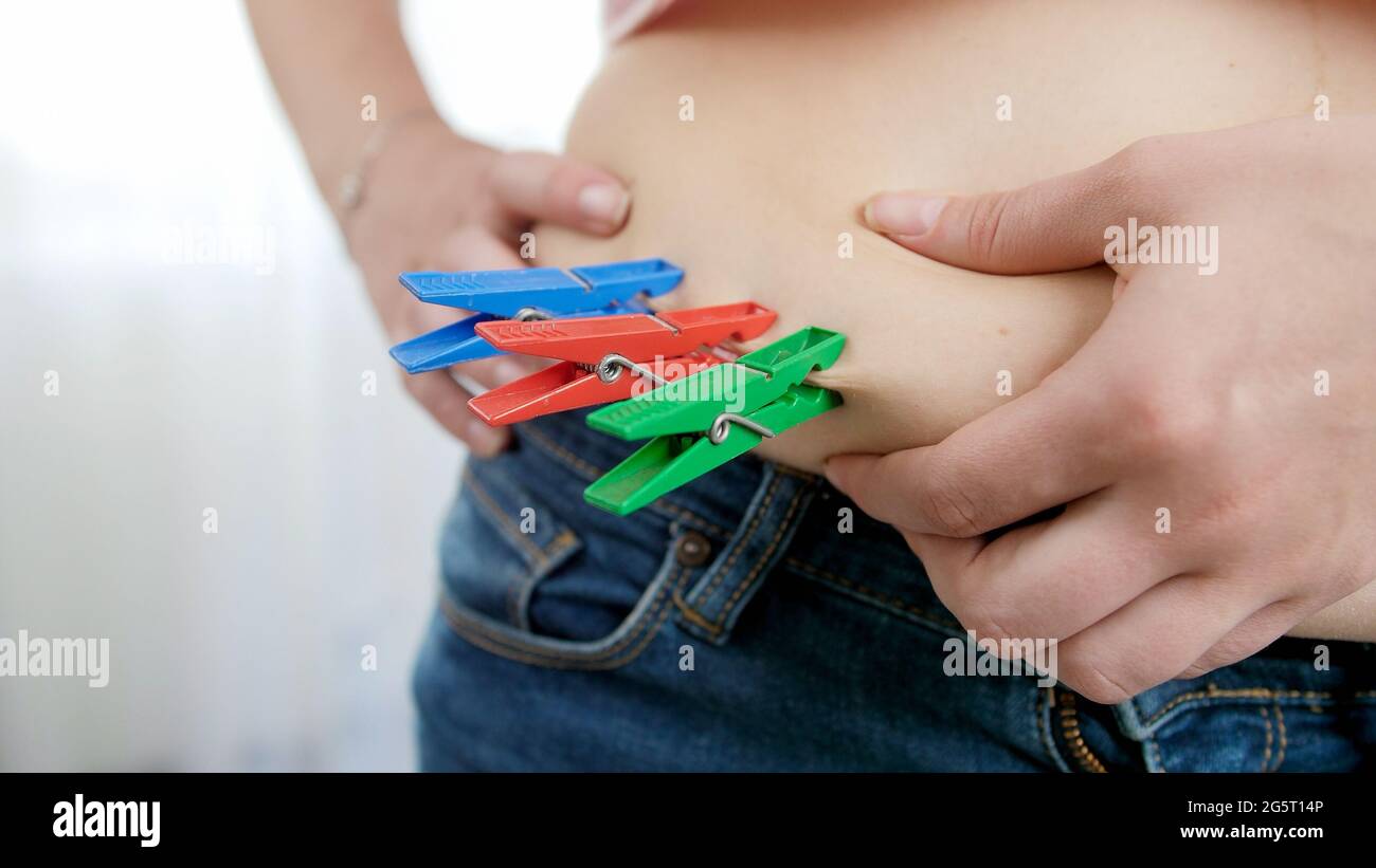 Young woman loosing weight hanging clothespins on her big belly ...