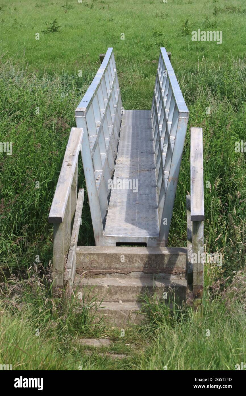 Concrete steps and wooden handrail leading up to a metal footbridge ...