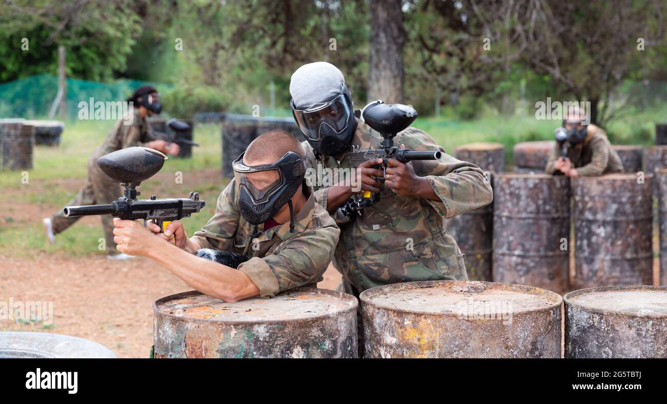 Two paintball player in camouflage and mask aiming with gun in shootout ...