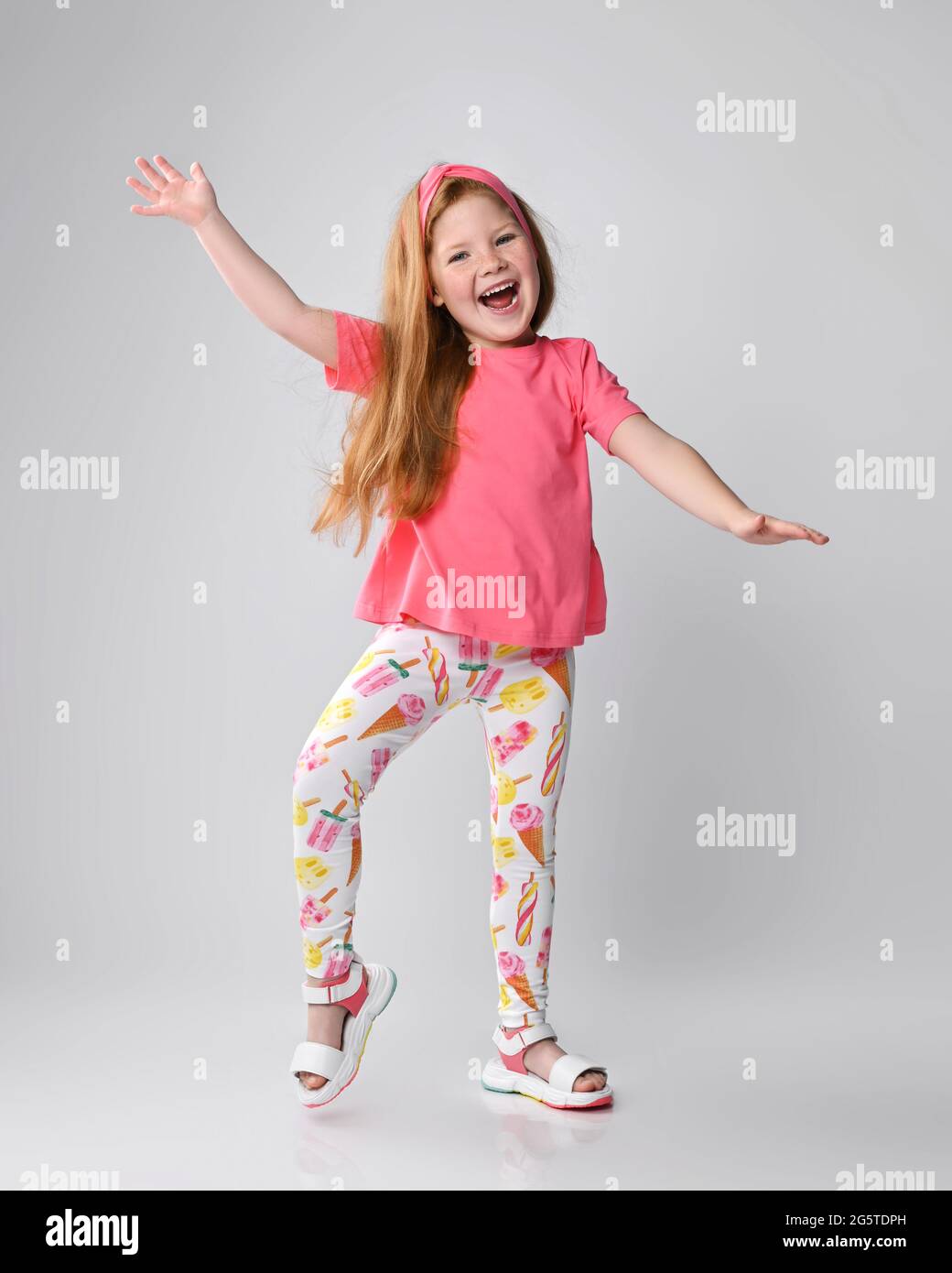 Happy active redhead kid girl in pink t-shirt, colorful pants and ...