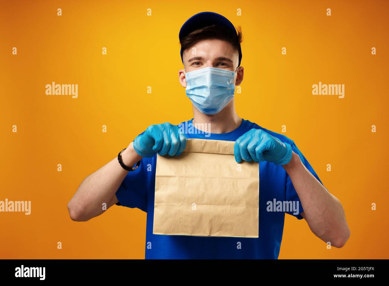 Young delivery man in face mask and gloves holding food delivery parcel ...