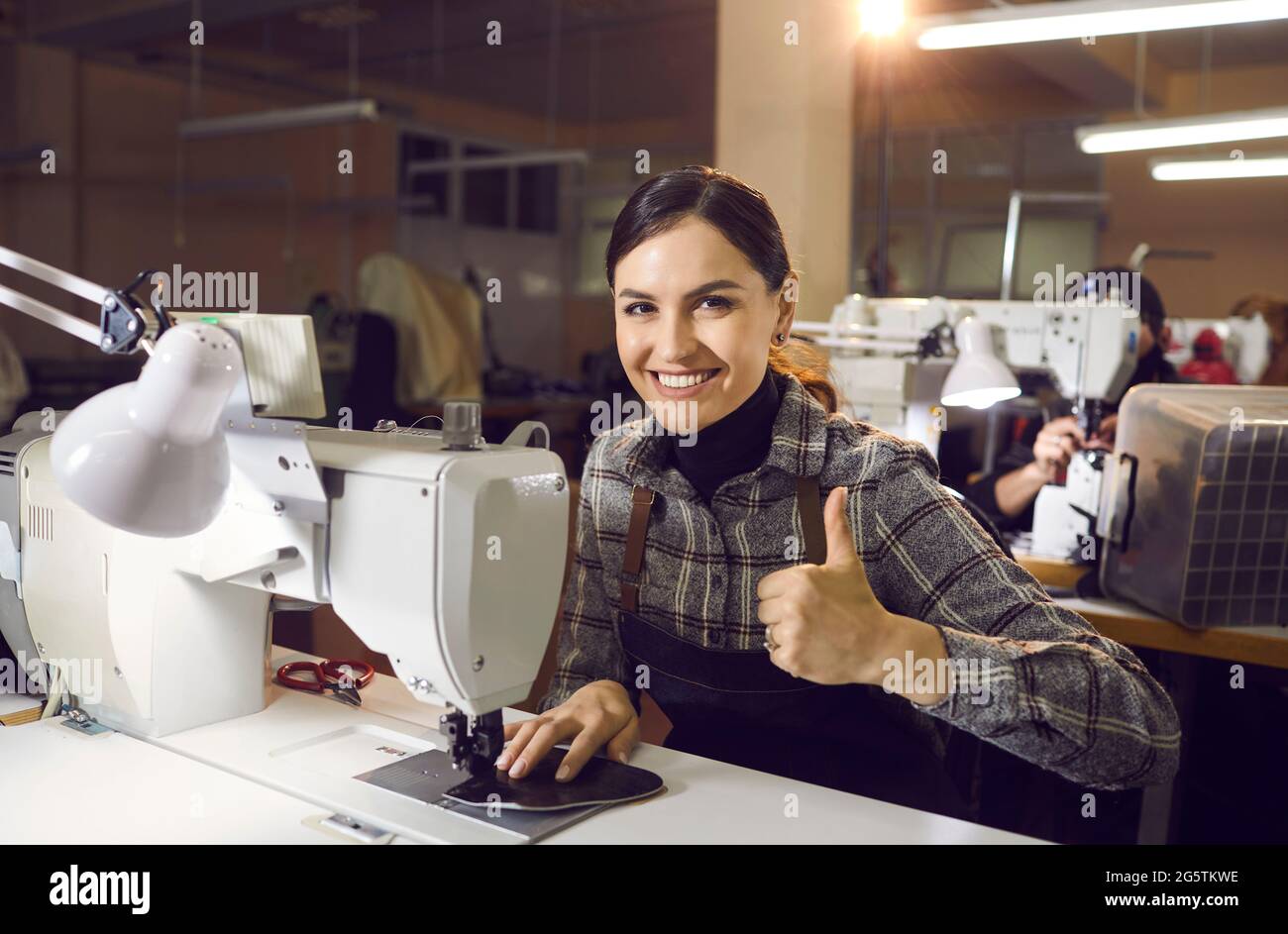 Satisfied factory worker sitting at shoe sewing machine, giving thumbs ...