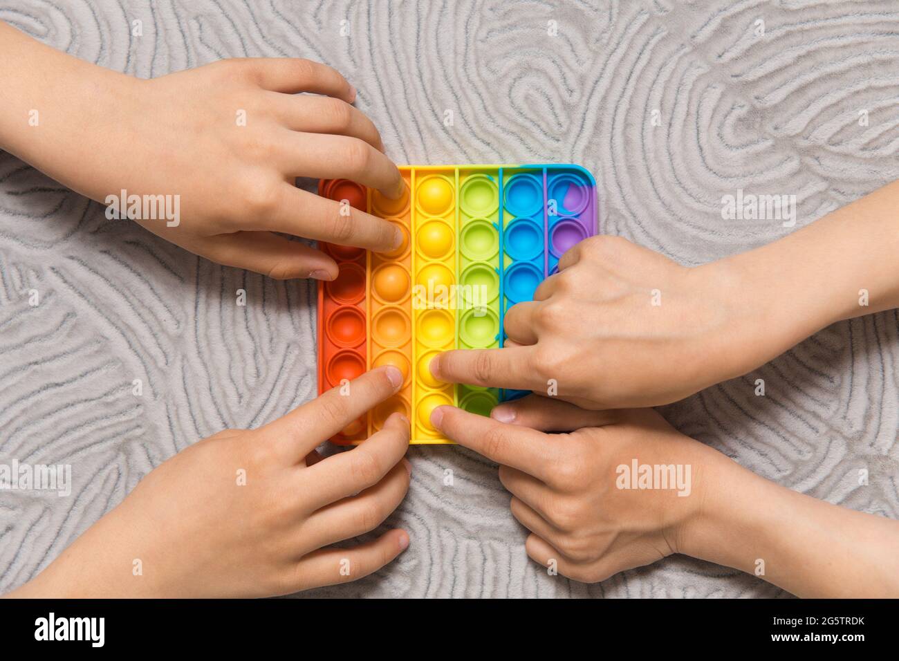 Two kids push sensory popit at the same time on gray background ...