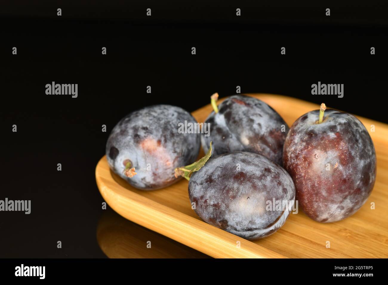 Four ripe dark purple plums on a wooden plate, close-up, isolated on a ...