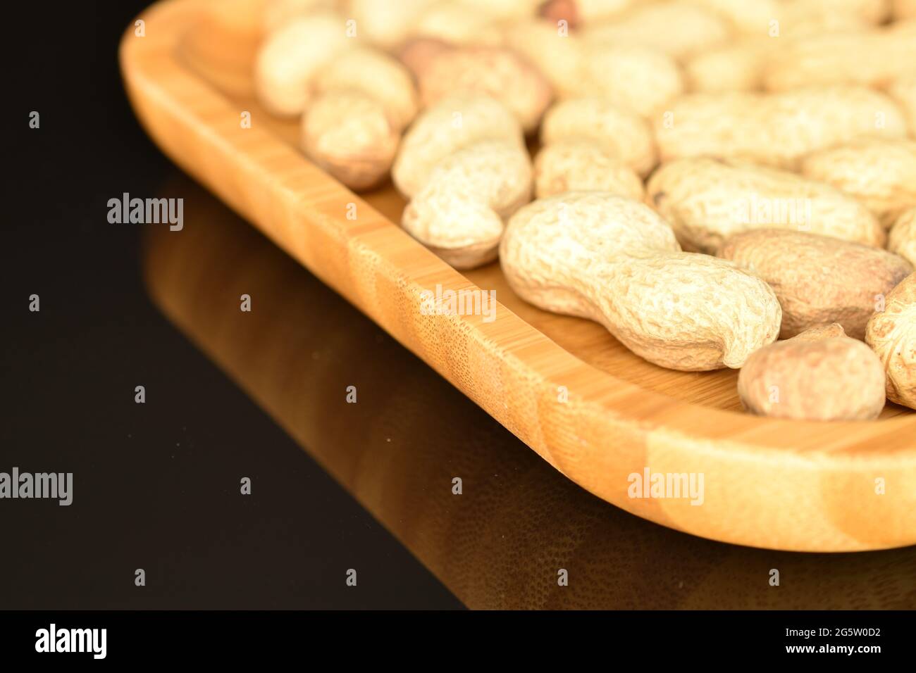 Organic unpeeled peanuts in a bamboo plate, close-up, isolated on a ...