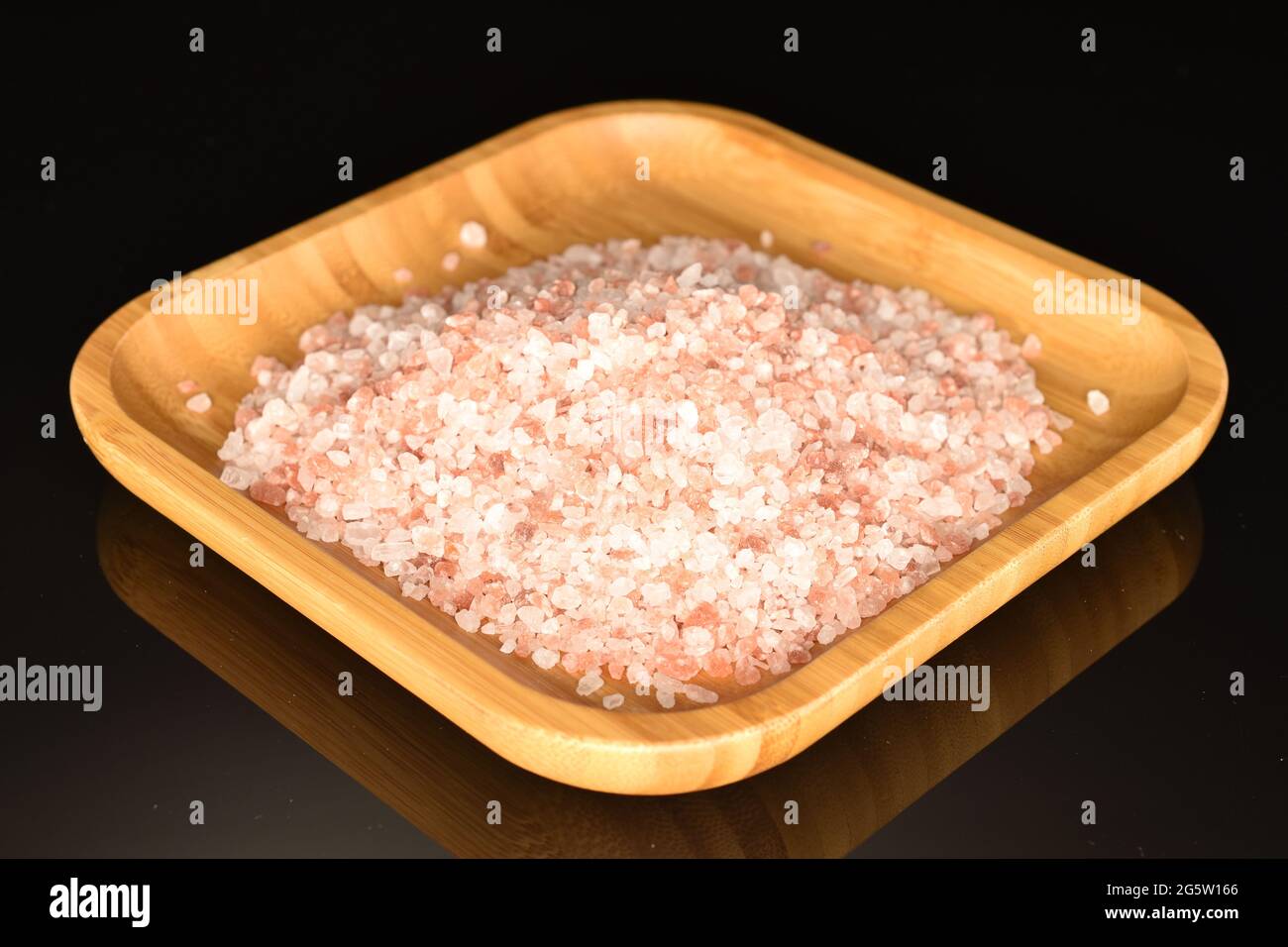 Rock salt of pink color in a bamboo plate, close-up, isolated on black ...