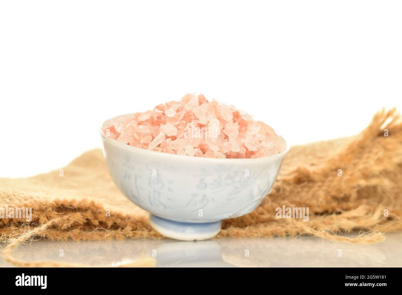 Rock salt of pink color in a ceramic salt shaker with a jute napkin ...