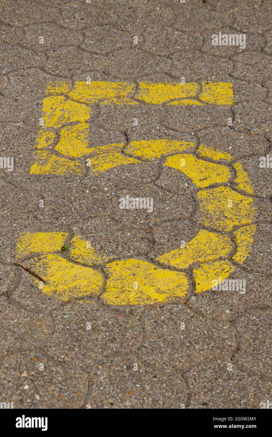 Yellow number 5 painted on concrete paving stones Stock Photo - Alamy