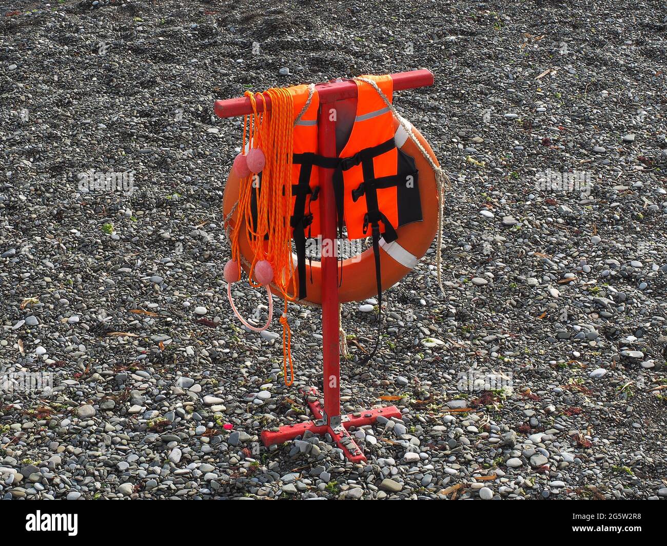 Lifebuoy and lifejacket hang on metal stand on a pebble beach Stock ...