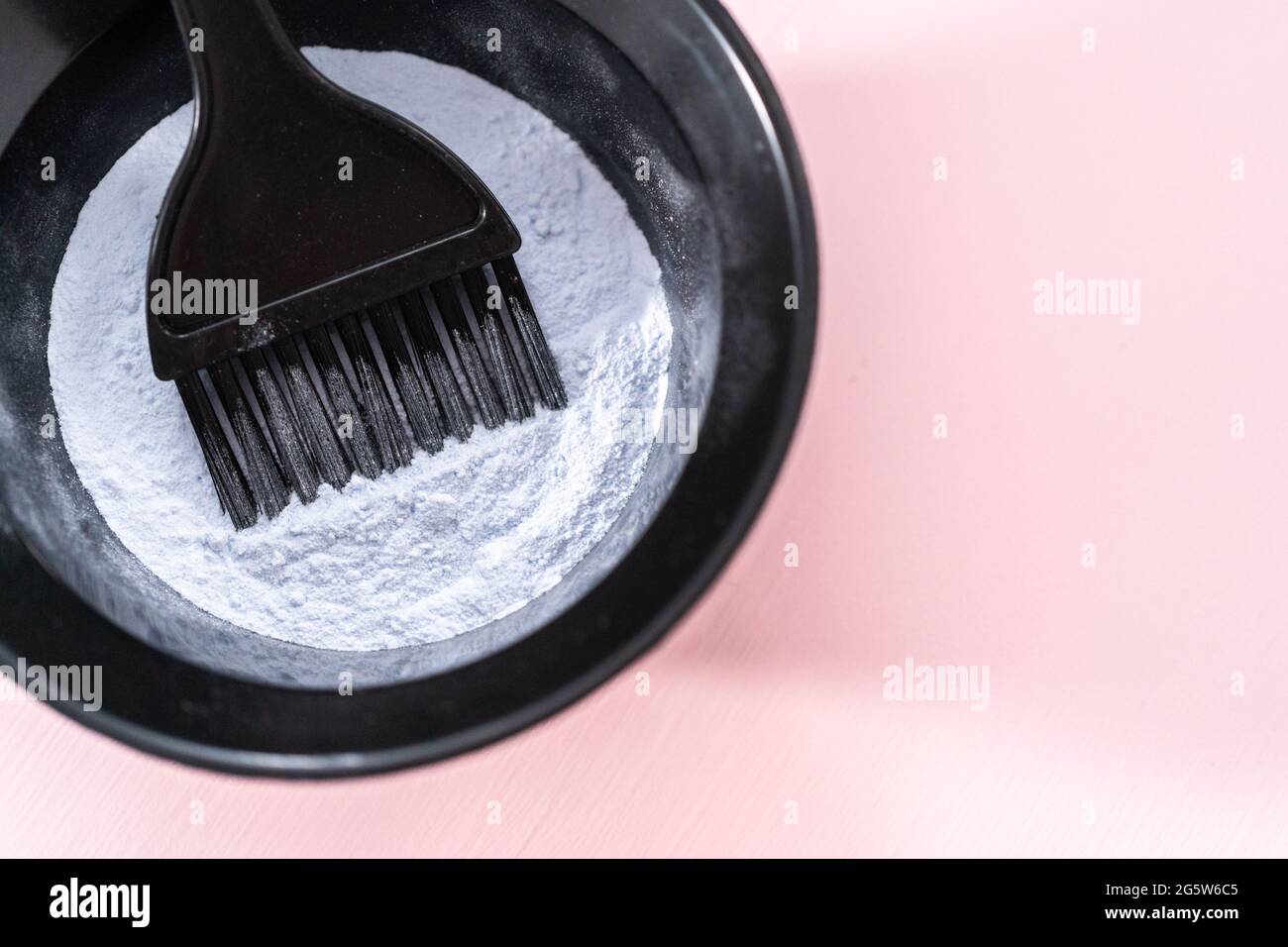 Hair color dye powder in a black plastic mixing bowl on a pink ...