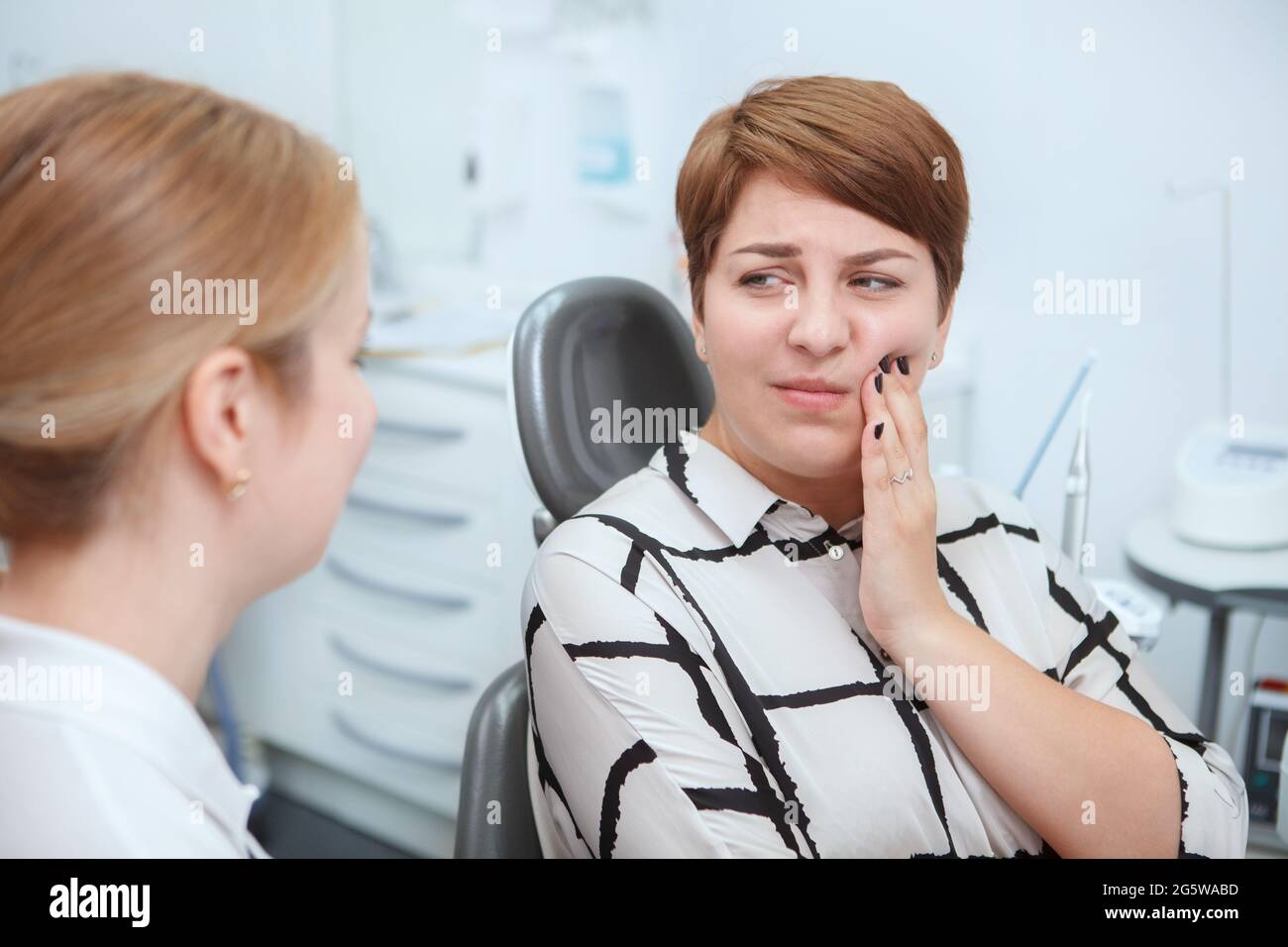 Young woman having toothache, sitting in dental chair at the clinic ...