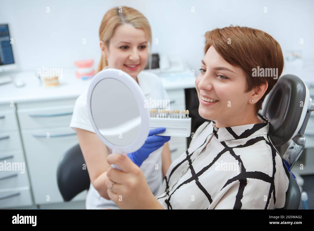 Happy young woman checking teeth in the mirror after teeth whitening ...